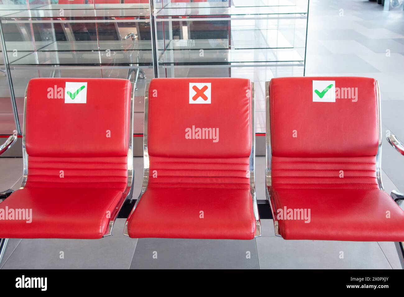 Three red airport chairs have social distancing signs. The middle chair ...