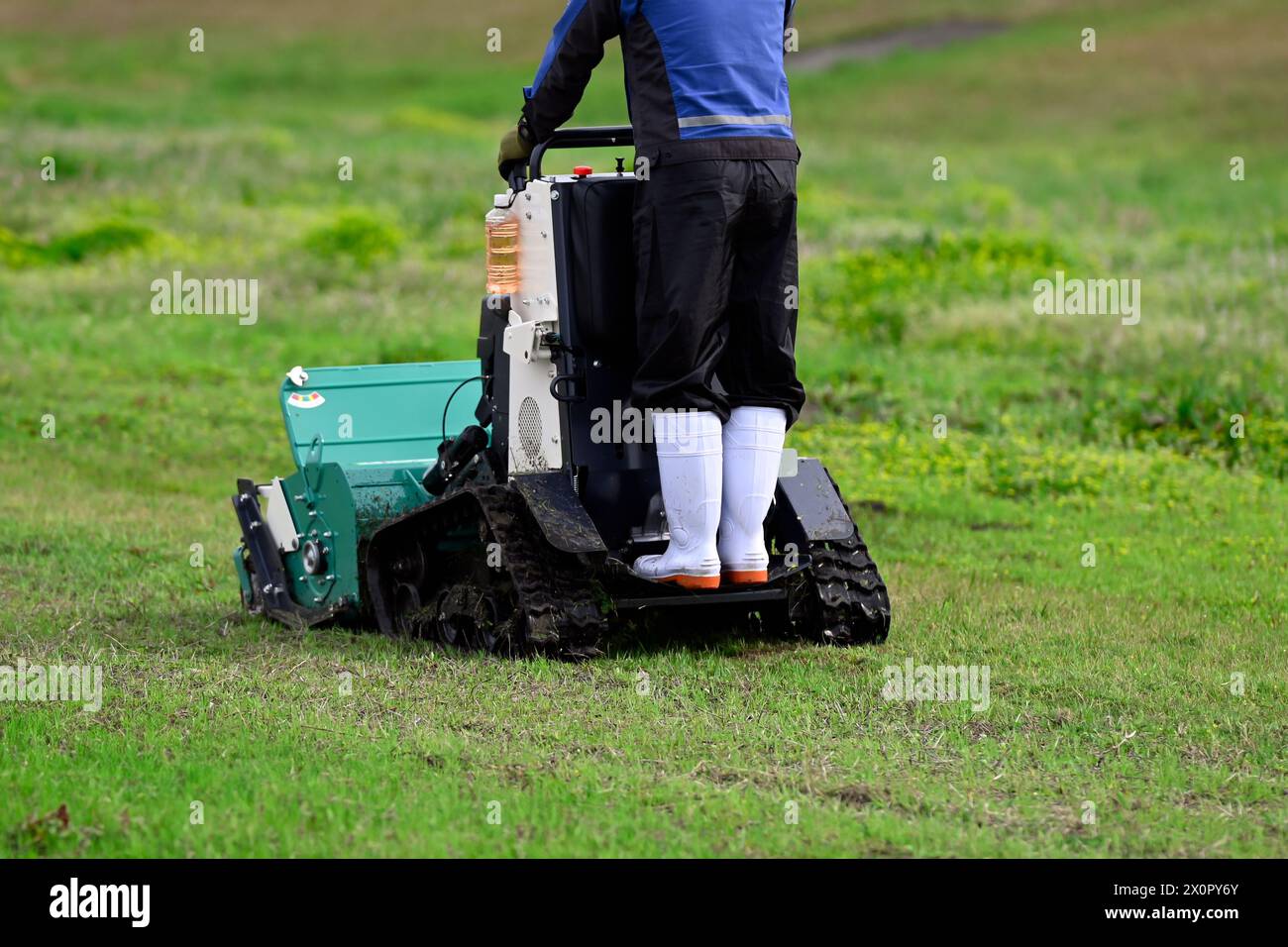 A person riding and operating a flail mower to mow the grass in the ...