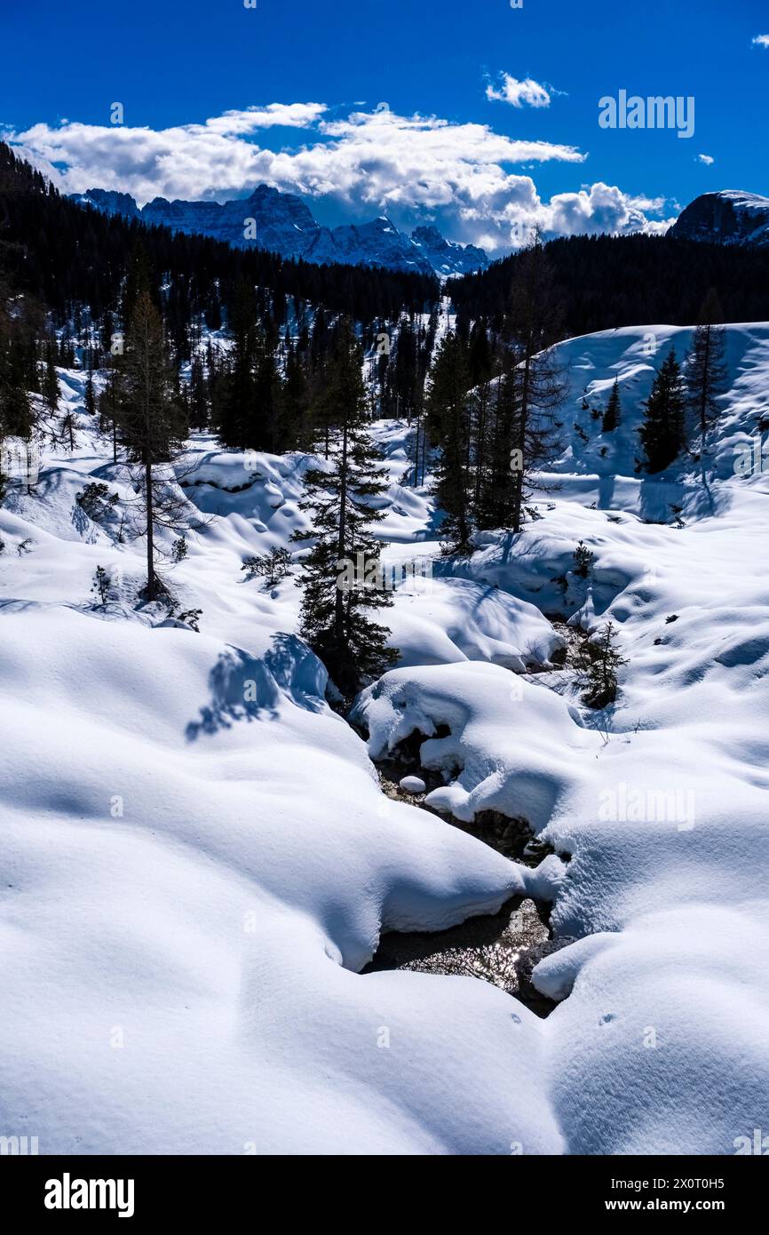 Snow-covered slopes of alpine Dolomite landscape with a small river and ...