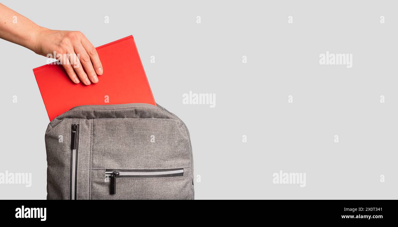 Hand putting red book, textbook into backpack, school bag. Banner ...