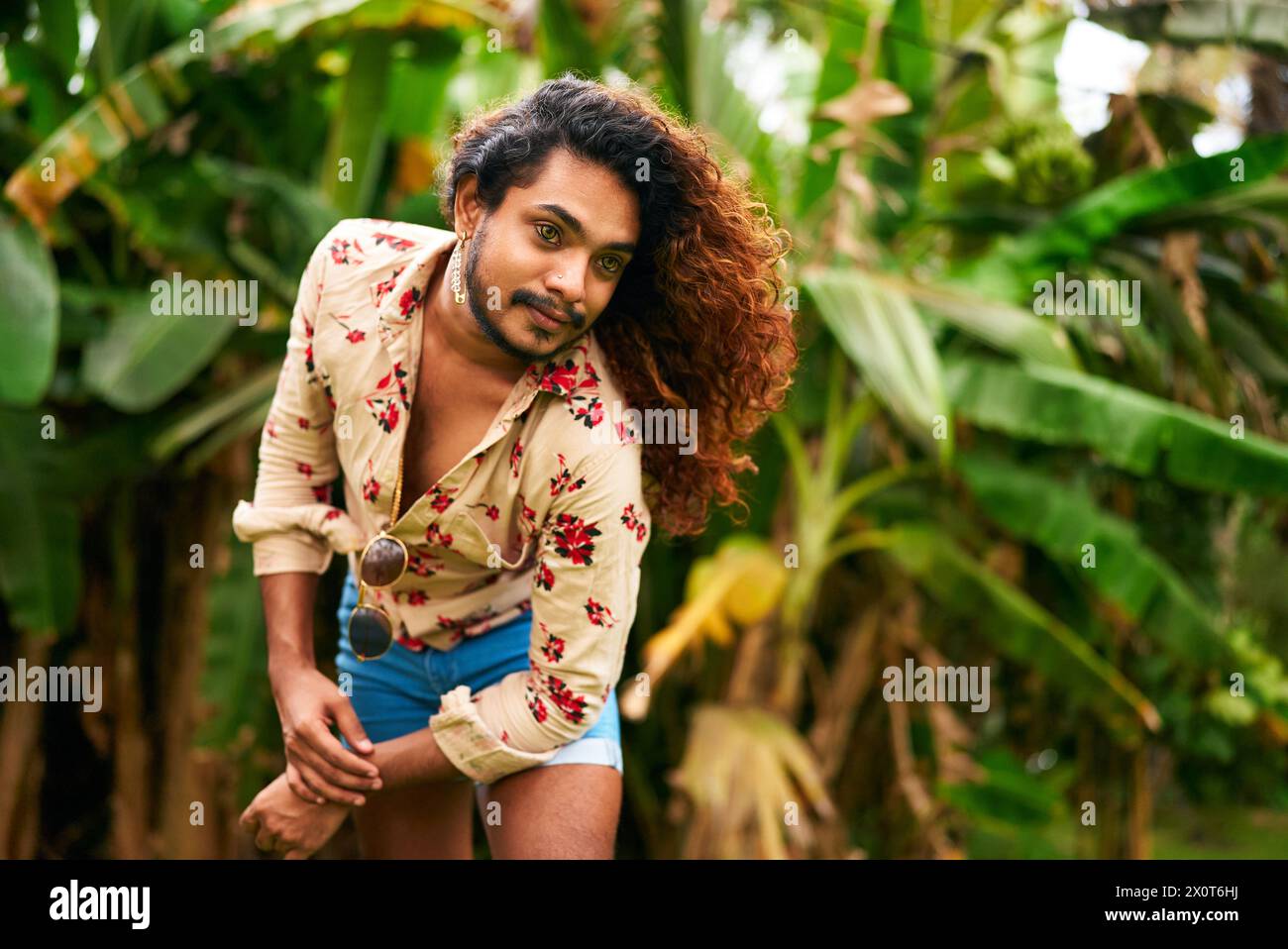 Confident gay man with curly hair in tropical setting poses with style ...