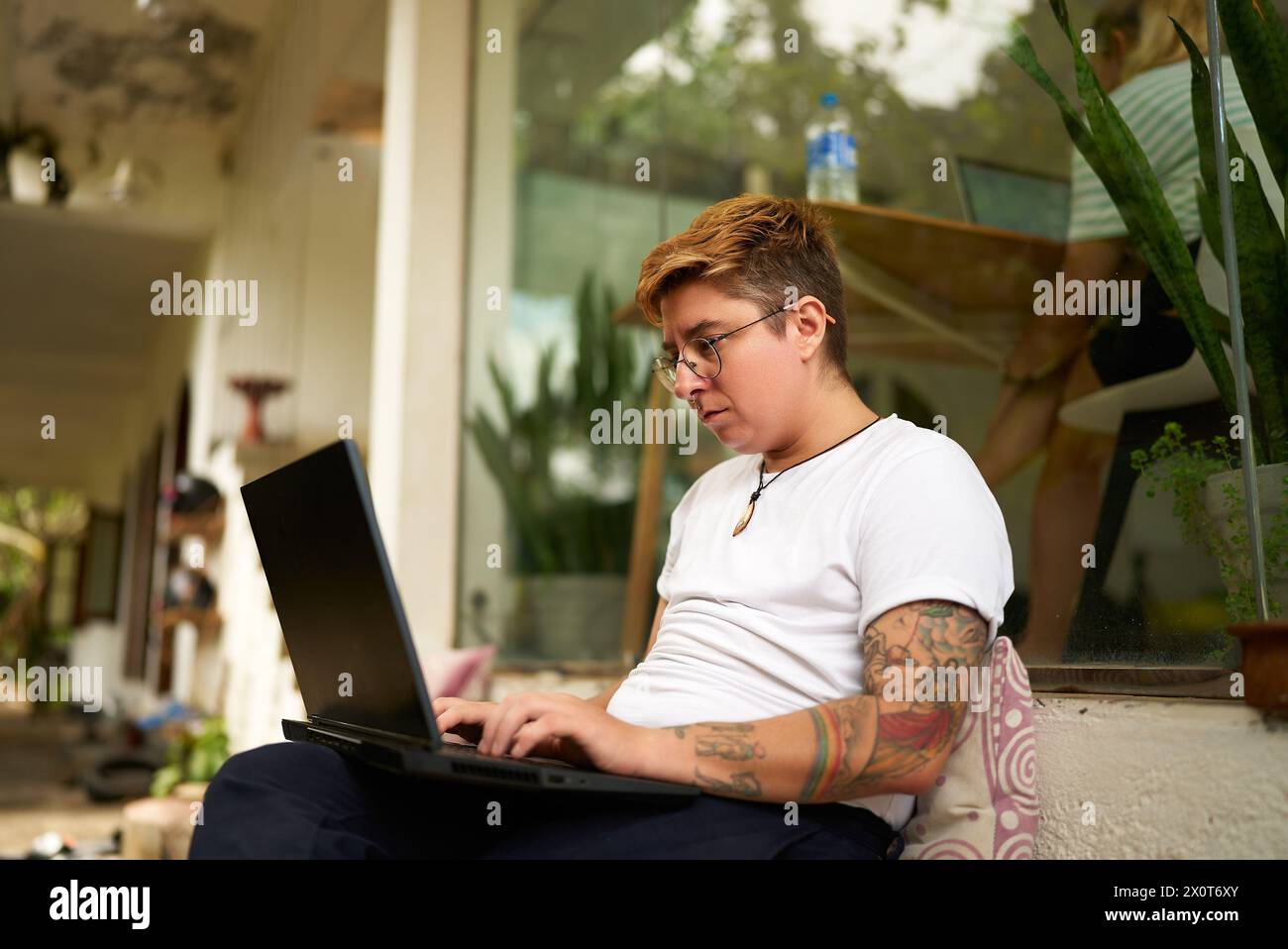 Transgender pro works on laptop outdoors, focused on task. Relaxed ...