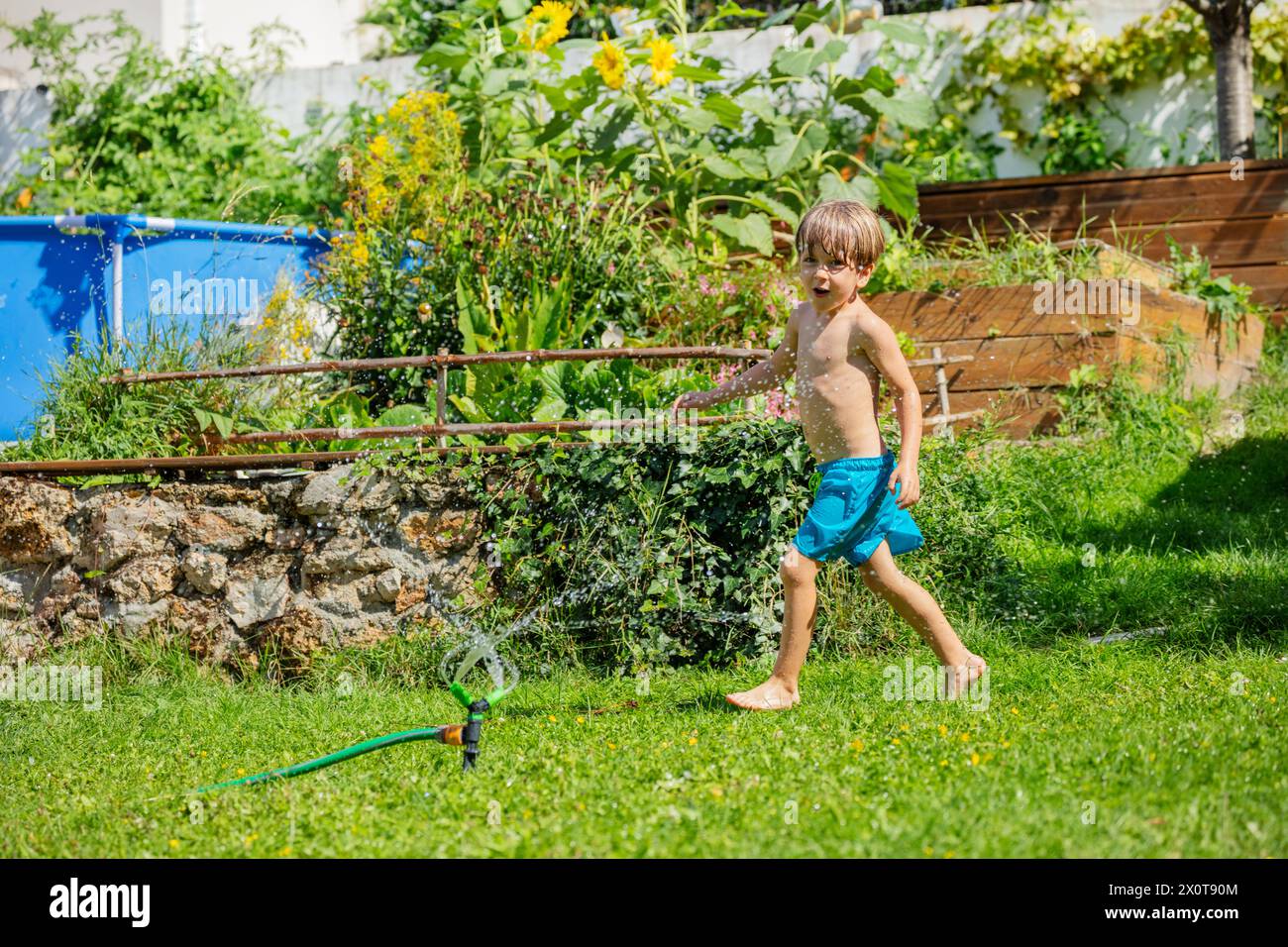 Happy boy frolics through spray of water from outdoor sprinkler Stock ...
