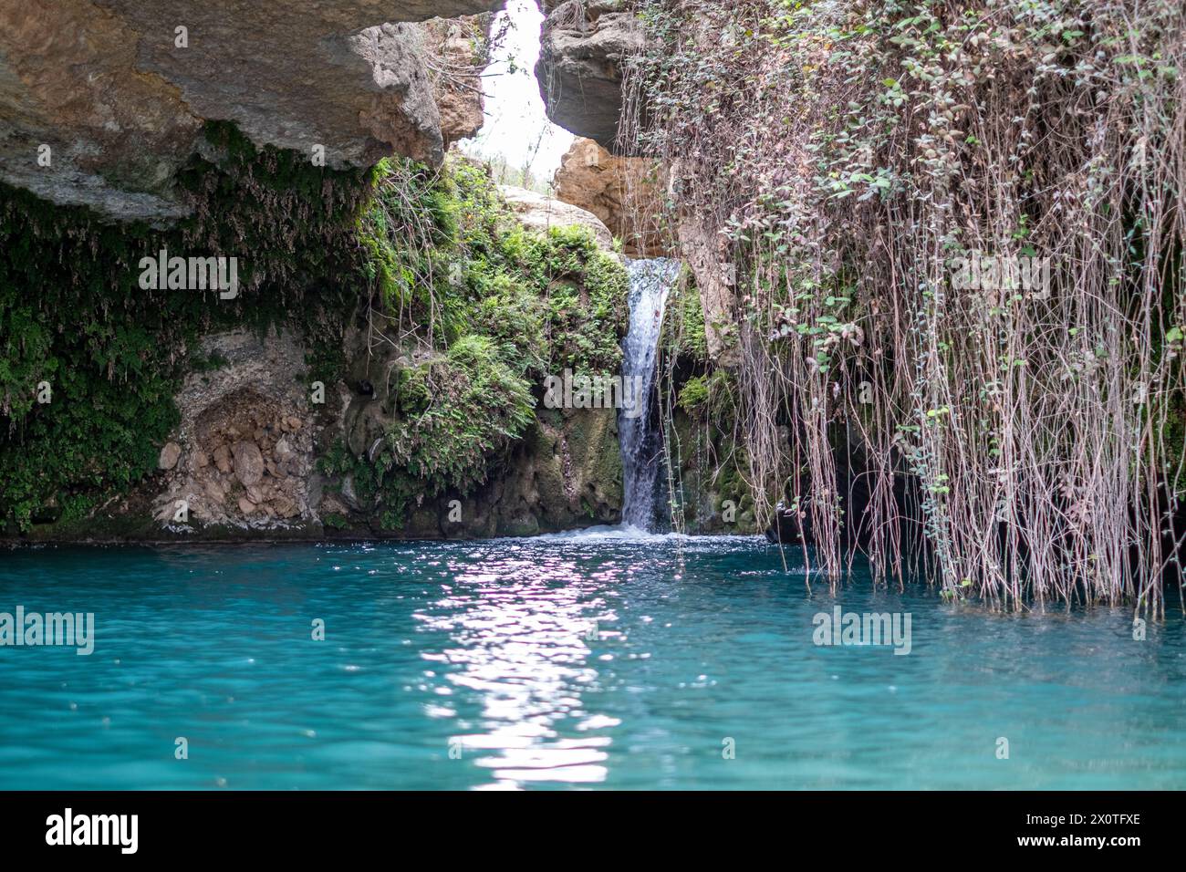 A secluded waterfall flows into a crystal clear blue lagoon, flanked by ...
