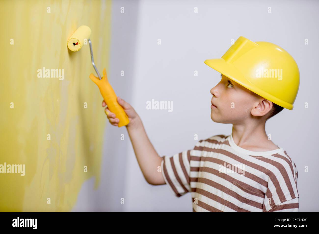 Cute boy with a paint roller. Happy kid helps parents to paint wall ...