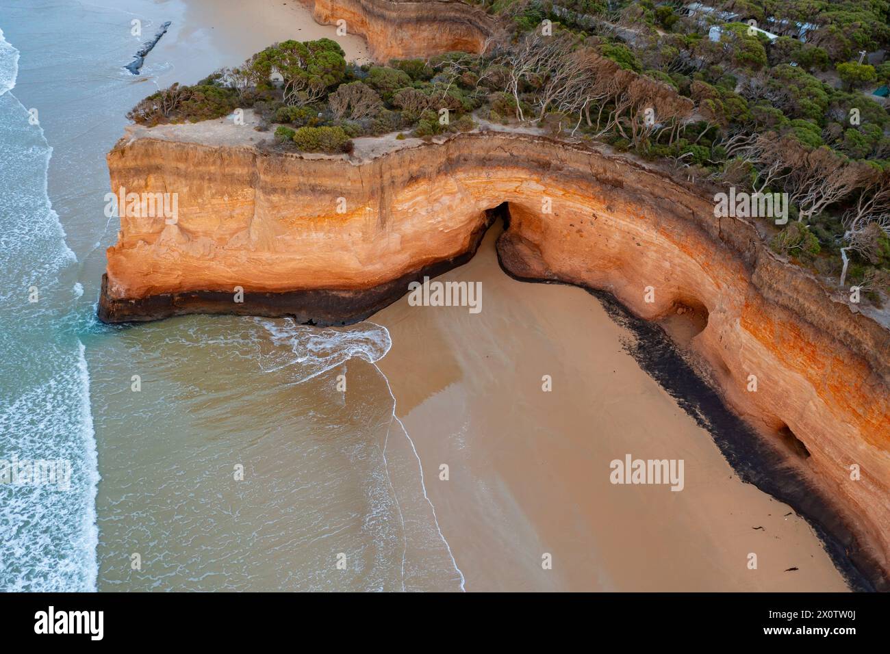 Aerial view of coastal cliff protruding out over a sandy beach at ...