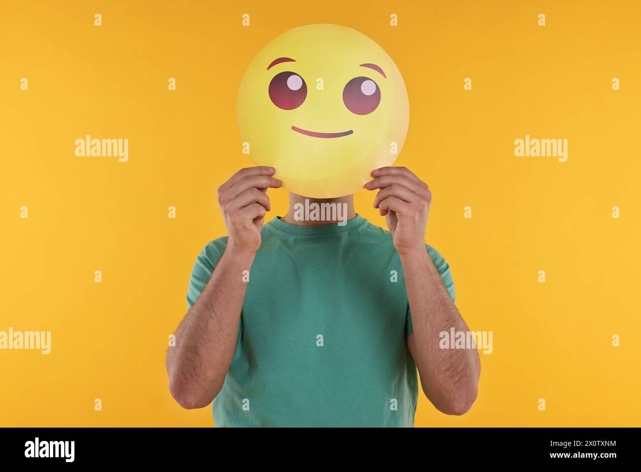Man covering face with smiling emoticon on yellow background Stock ...