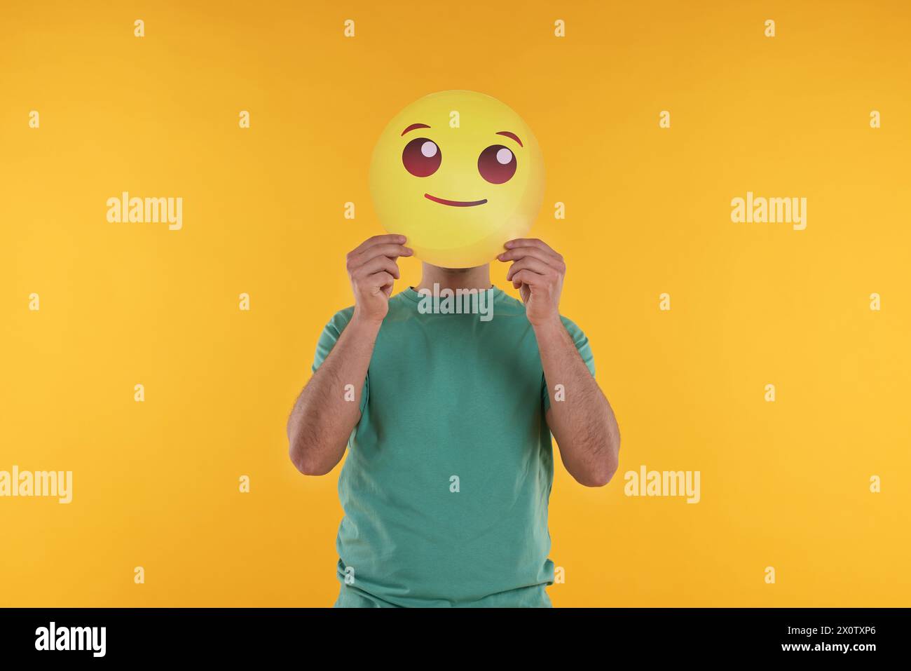 Man covering face with smiling emoticon on yellow background Stock ...