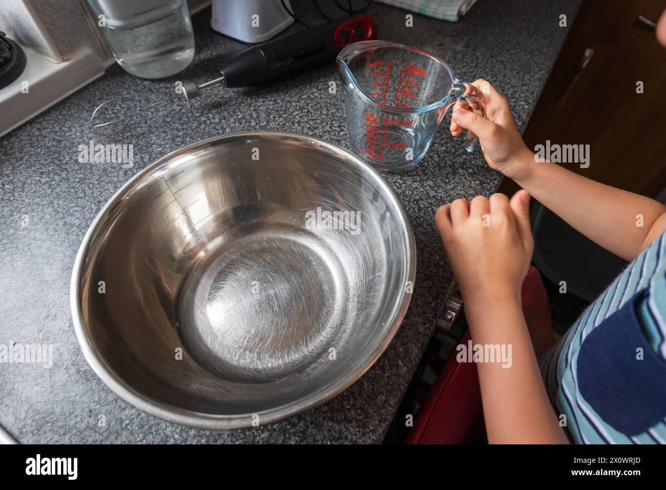 child standing at the kitchen countertop pouring a measuring cup into a ...
