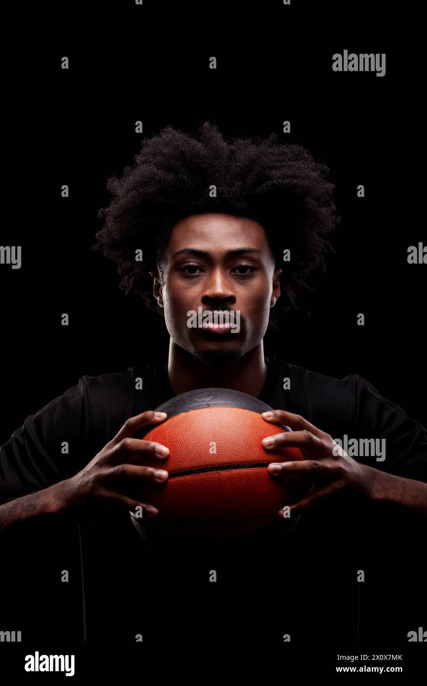Basketball player holding a ball against black background. Serious ...