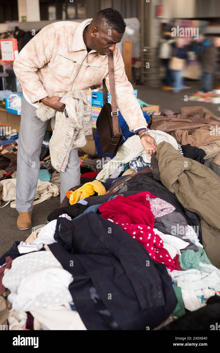 Ordinary african american guy chooses hands clothes at flea market ...