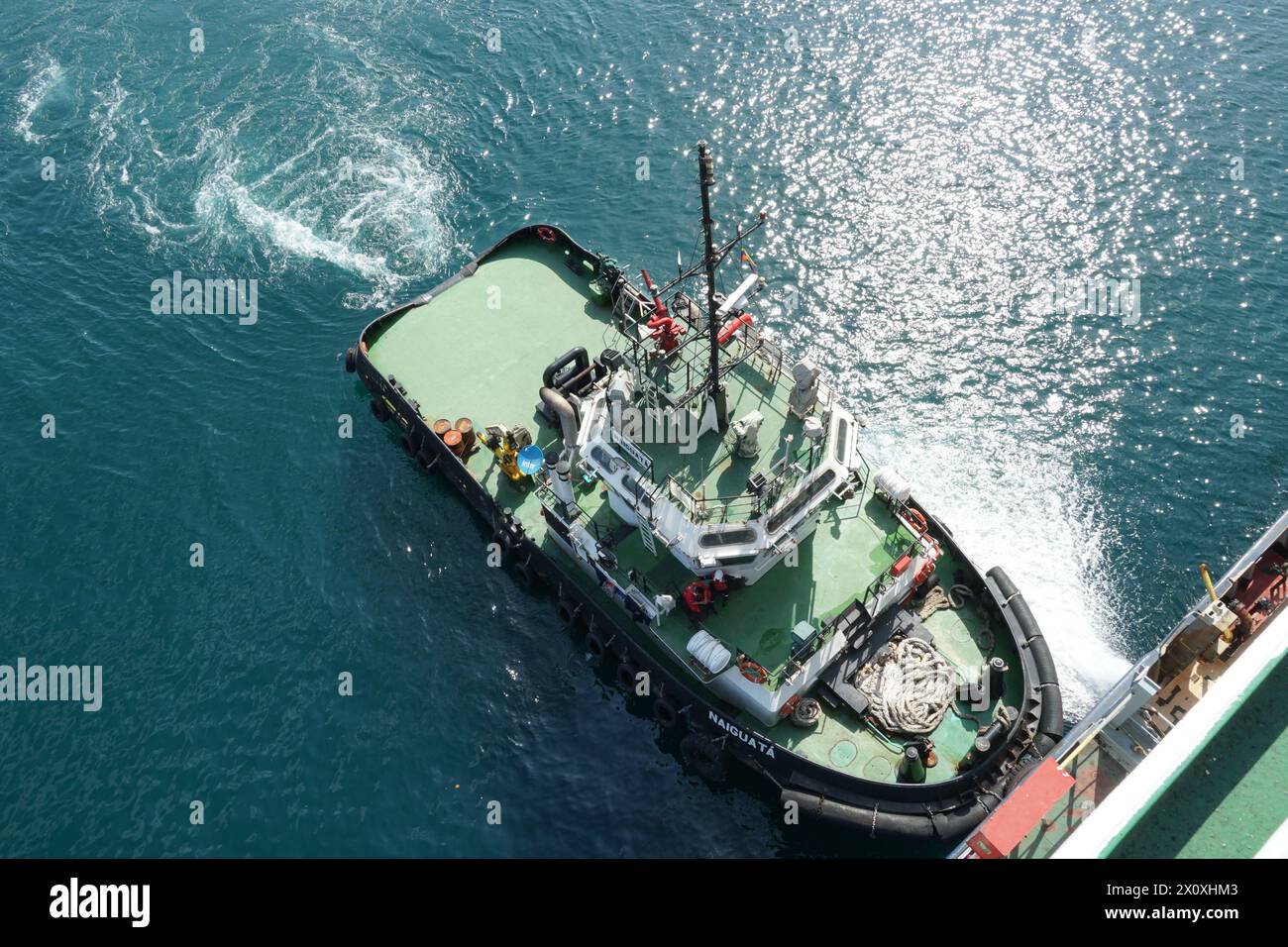 Pushing tug boat with green deck from side of hull of the container ...