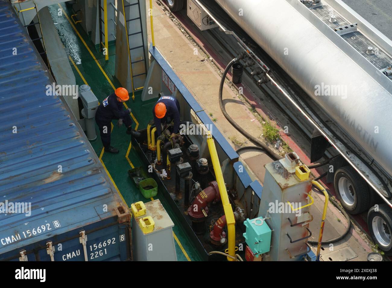 Tanker truck connected with fuel hose to container vessel in bunker ...