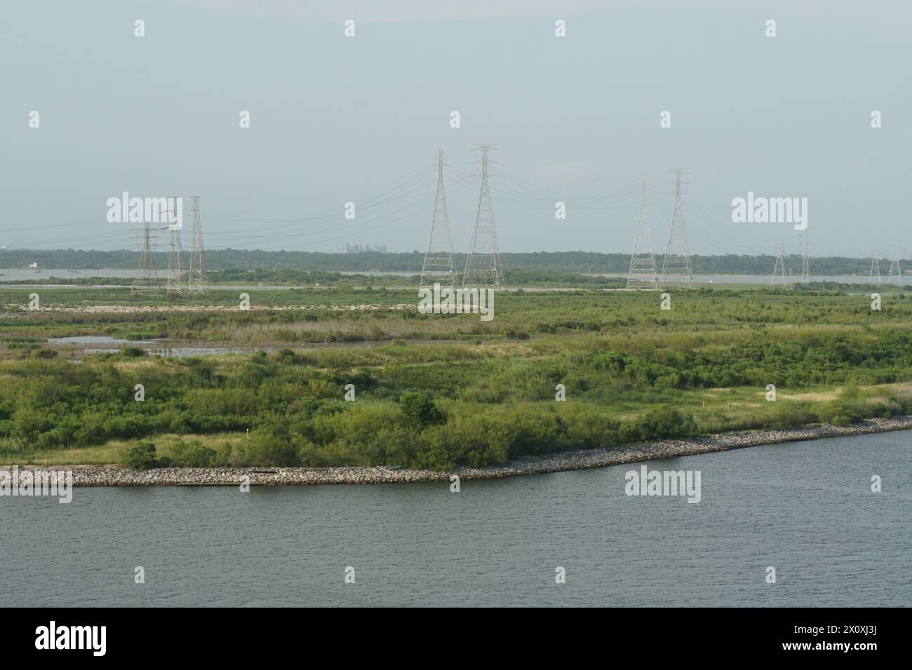 Tall electric pylons stretch across a green field and traverse through ...