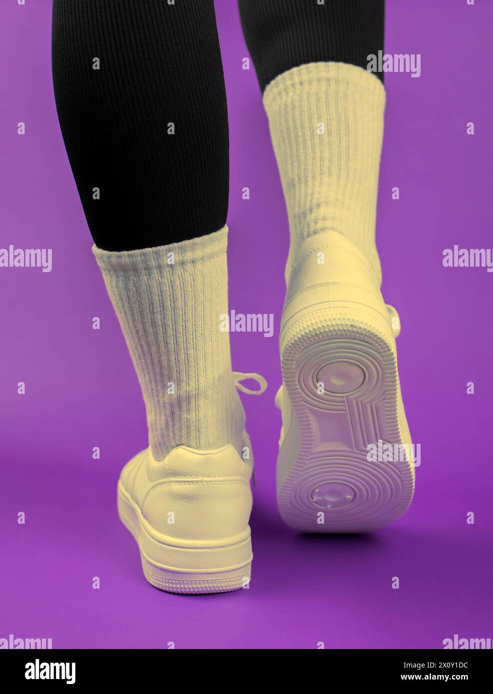 Close-up of female legs in white sneakers, back view, purple background ...