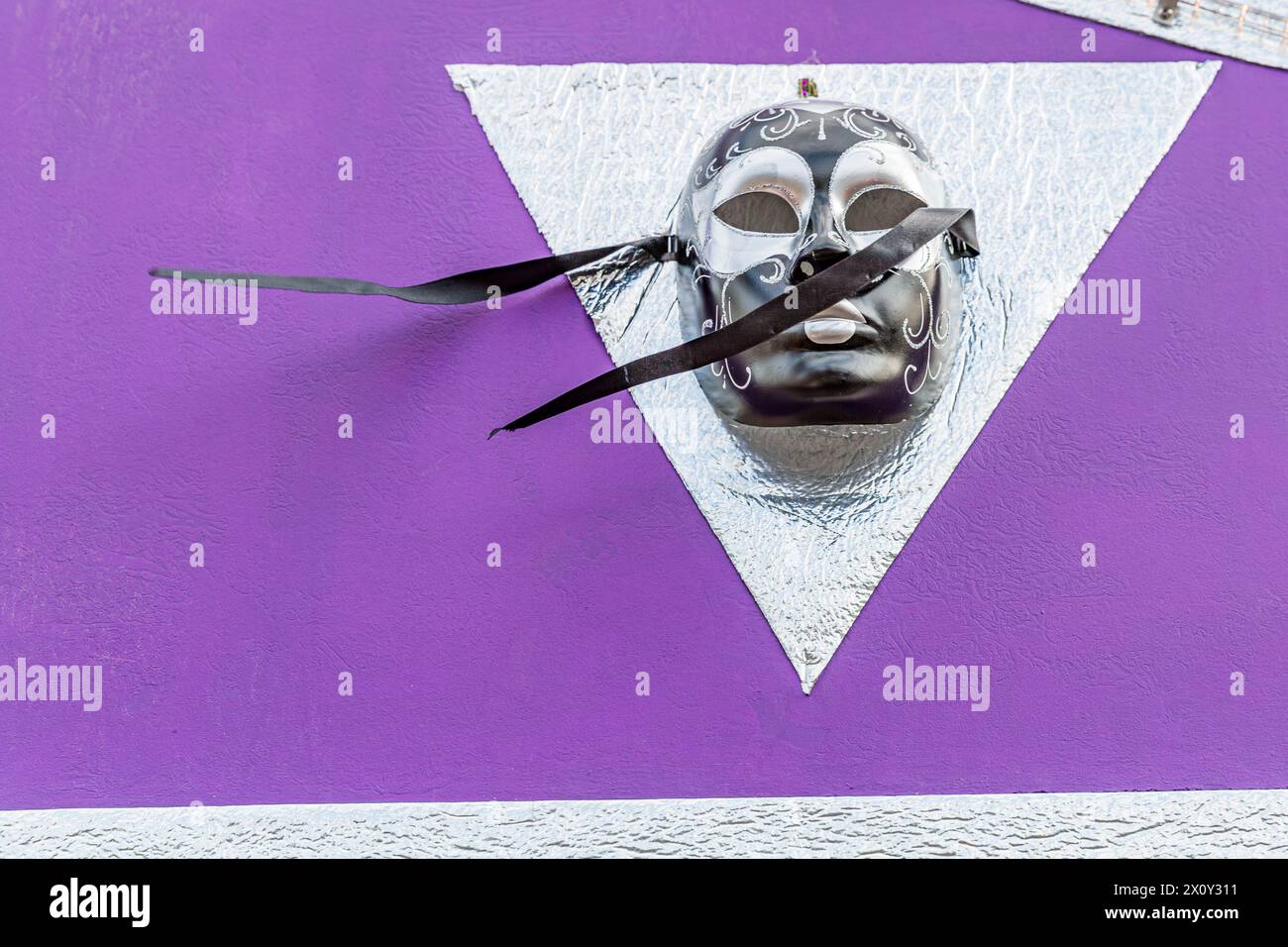 Gray mask with black details hanging in silver triangle on violet ...