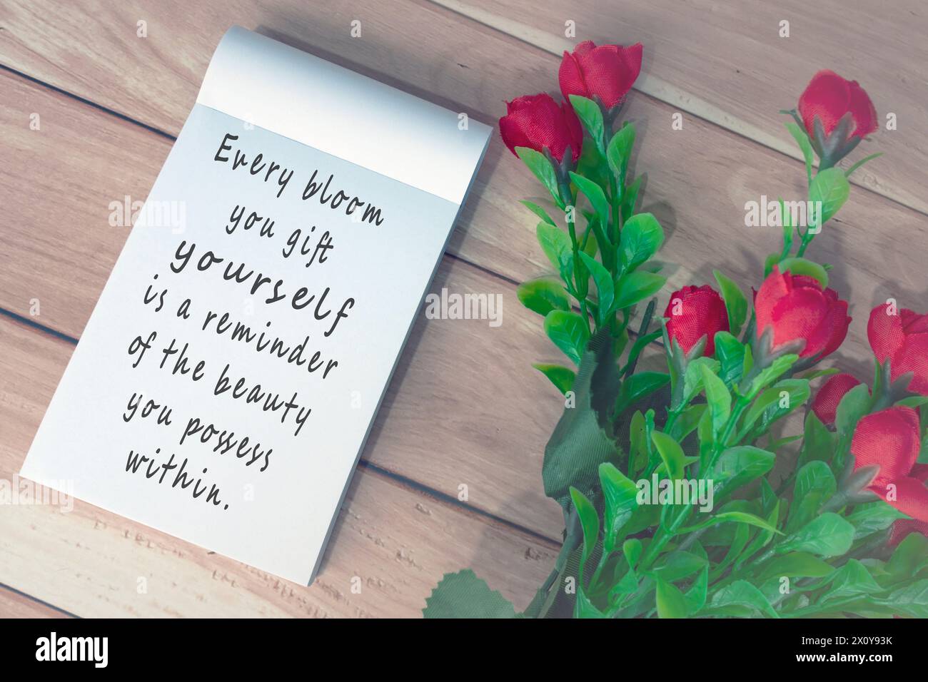 Motivational quote written on note book with artificial flowers on ...