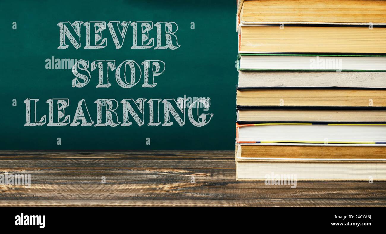 Never stop learning is written on a chalkboard with stacks of books behind it. The image conveys ...