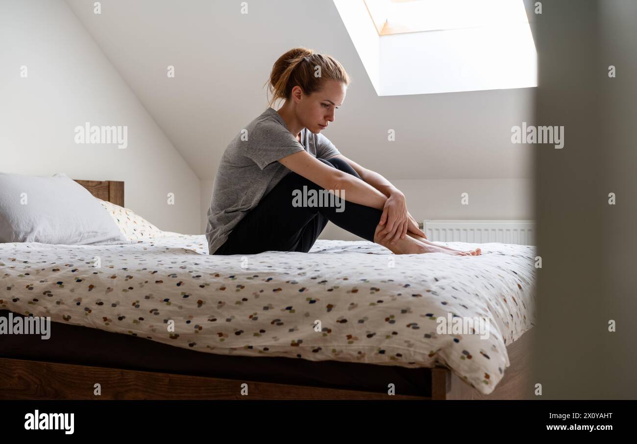 Upset unhappy lonely woman sitting alone on bed in bedroom. Mental ...