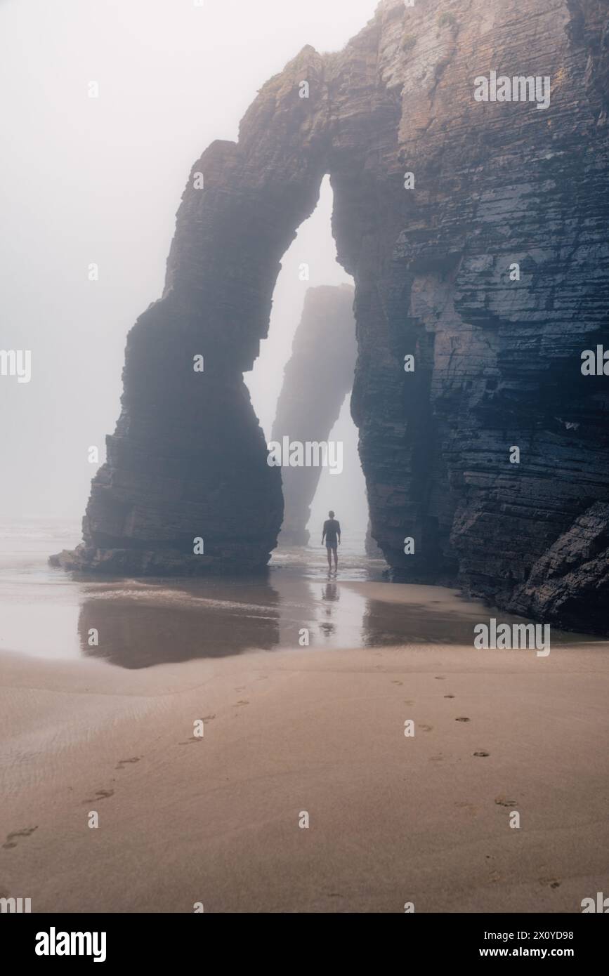 Man standing under natural arch on Cathedrals beach in Galicia, Spainn ...