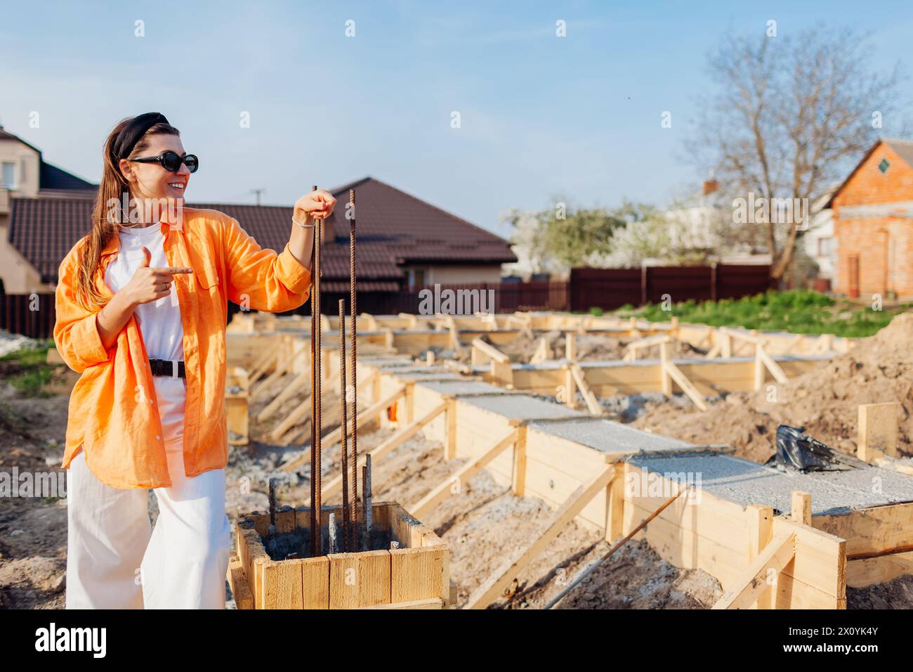 Concrete foundation for new house is done using wooden decking. Young happy woman owner pointing ...
