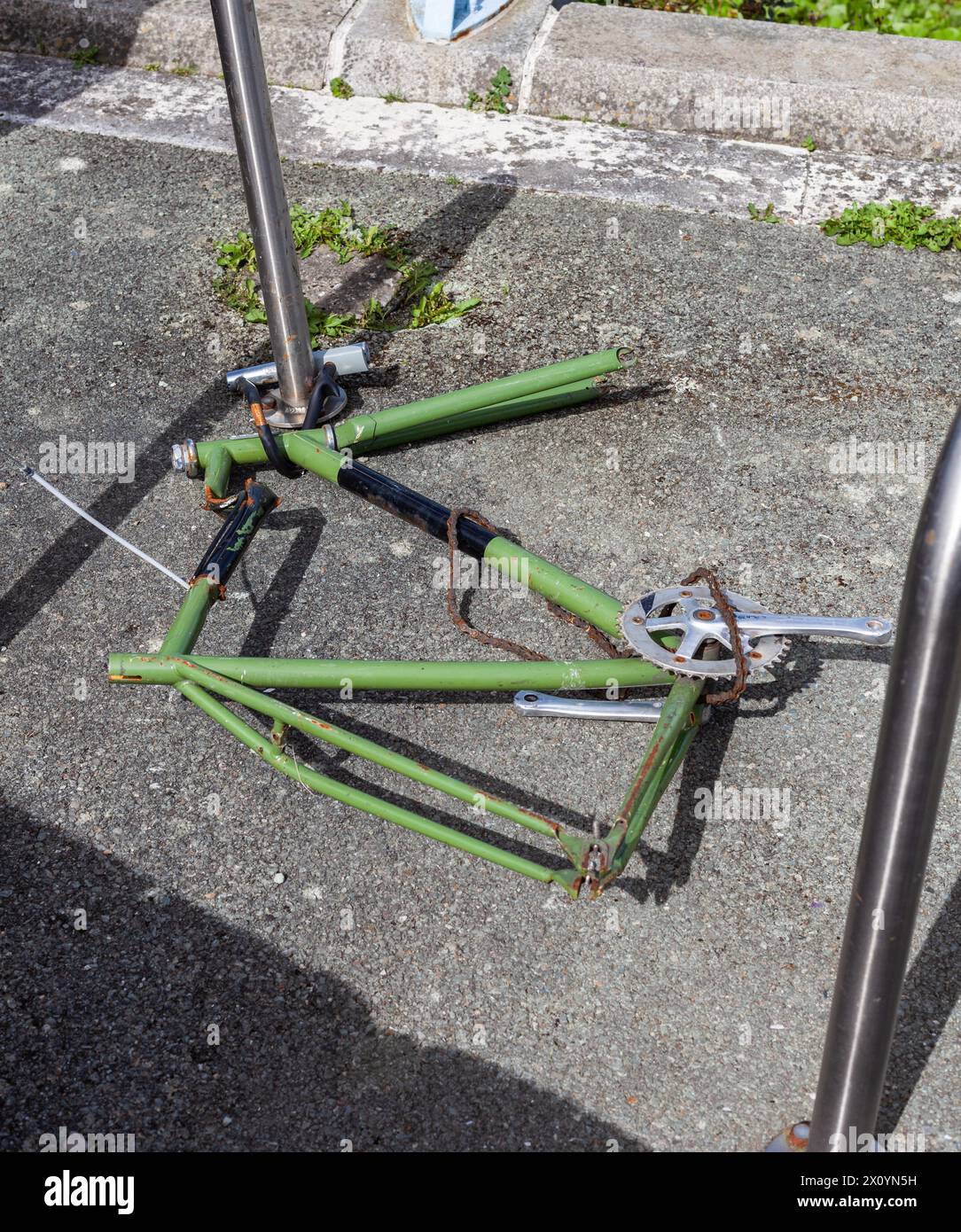 Green bicycle frame chained to a metal bar on the ground. The bike is ...