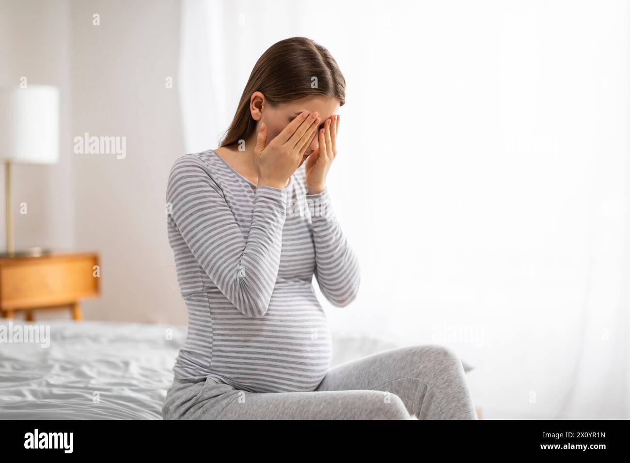 Sad pregnant woman sitting on bed covering face Stock Photo - Alamy