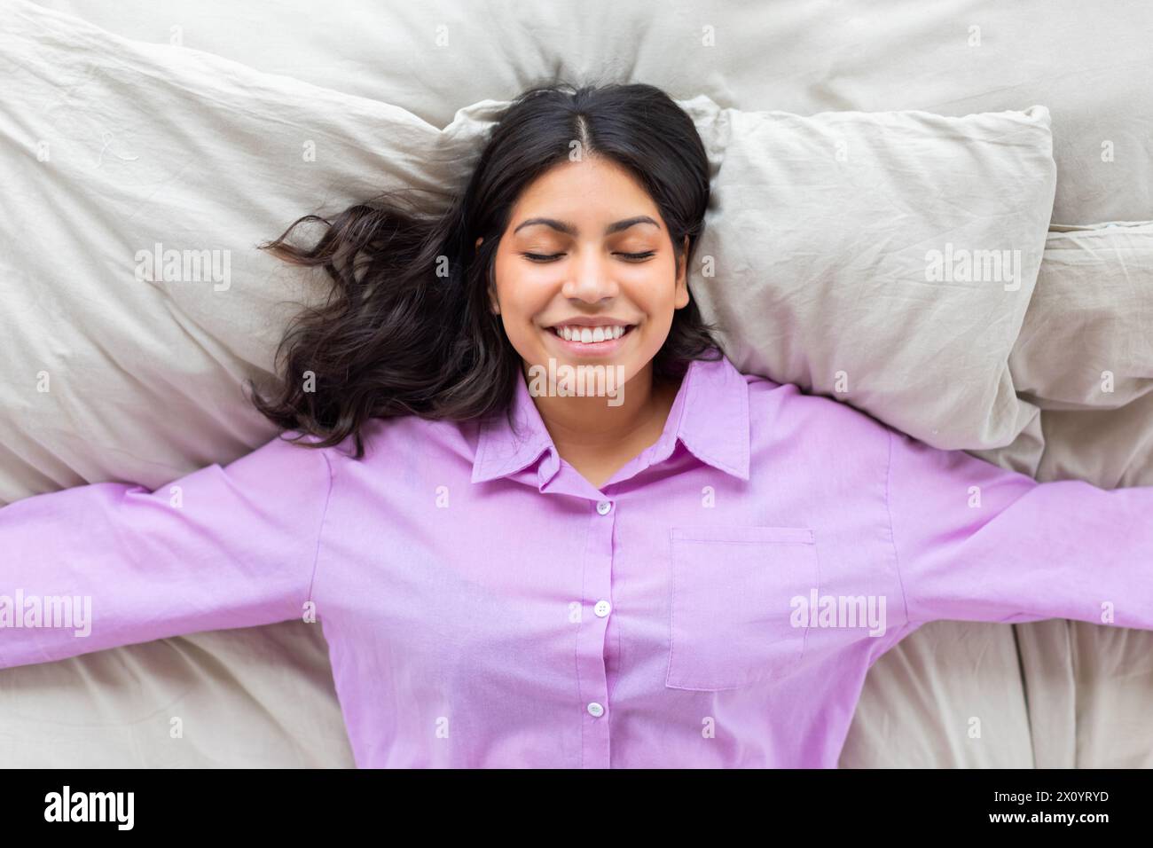Woman lying on bed with arms outstretched Stock Photo - Alamy