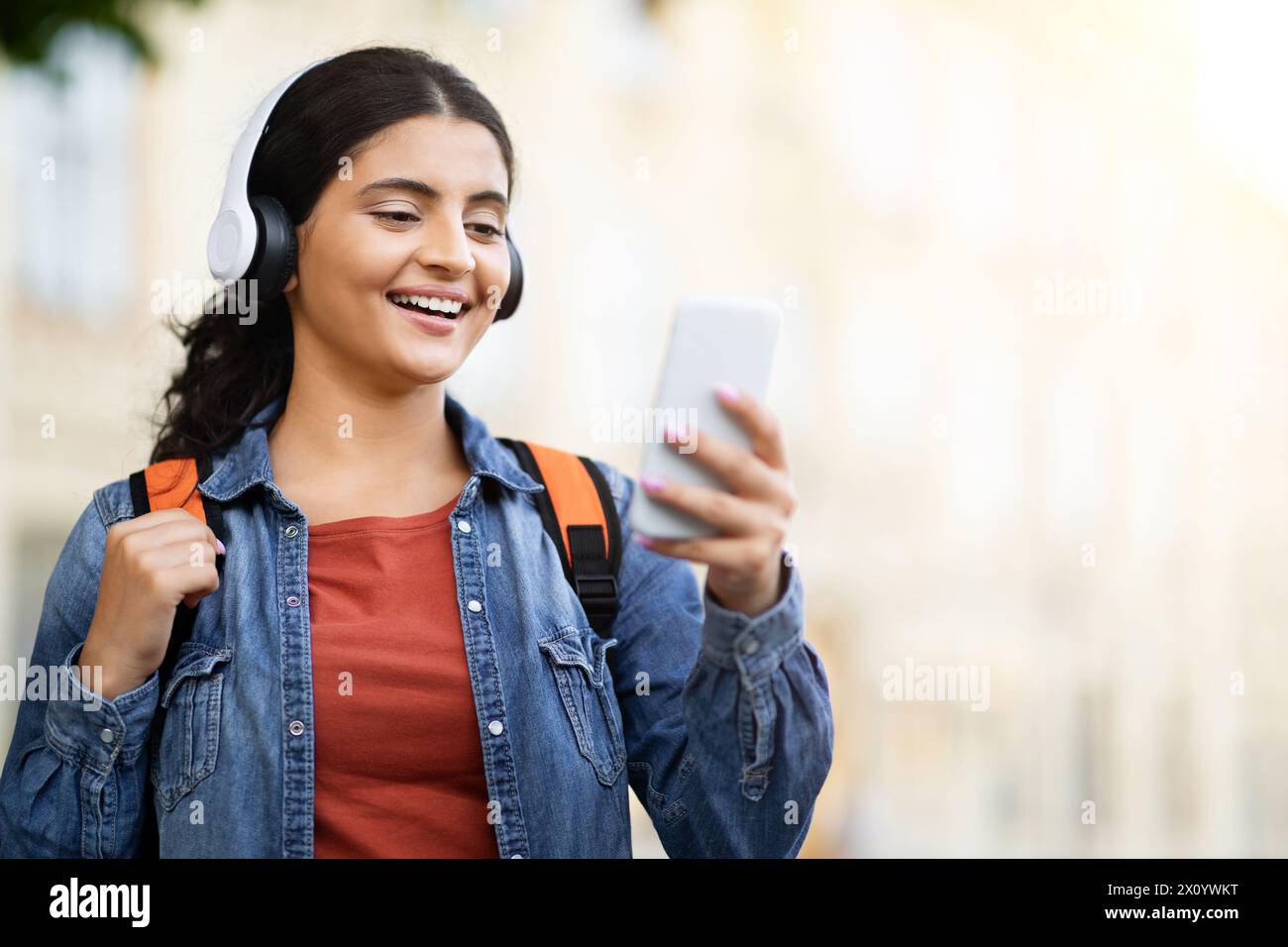 Indian student smiling with headphones, using phone Stock Photo - Alamy