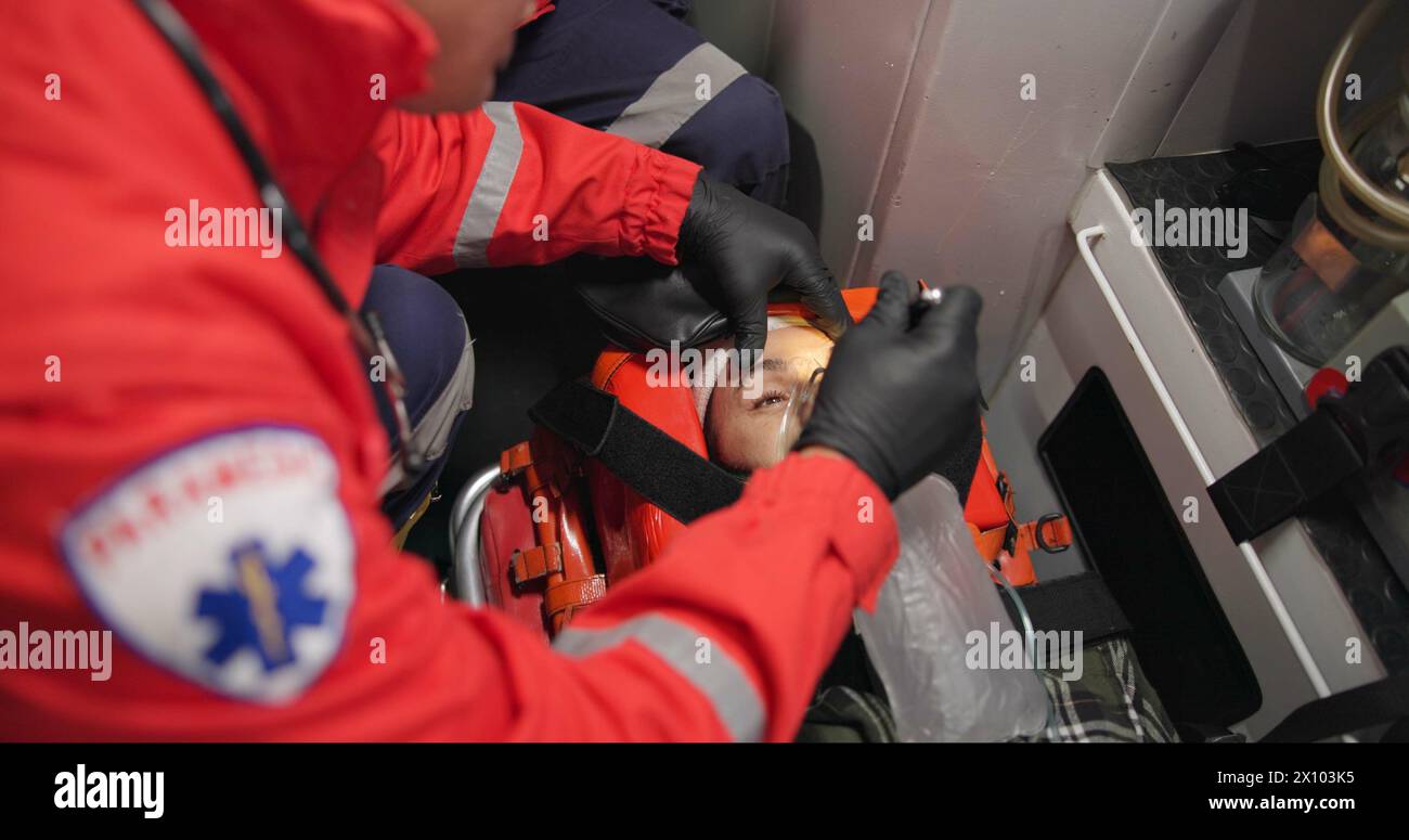Patient, paramedic and shine light into eyes to check pupil, test and ...
