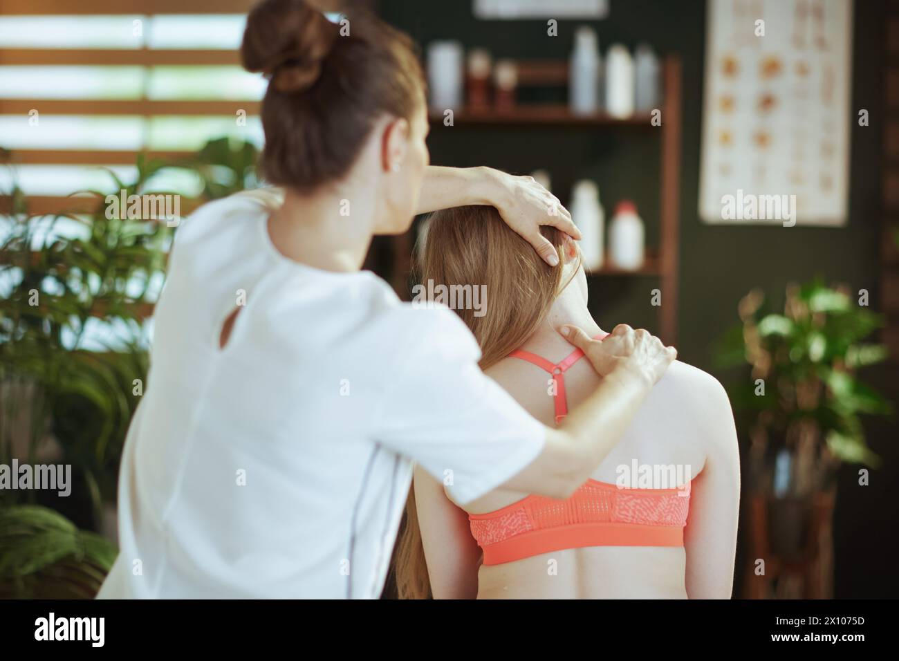 Healthcare time. Seen from behind female medical massage therapist in massage cabinet with ...