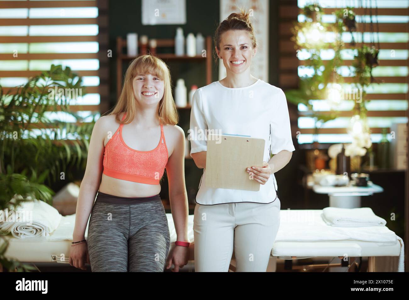 Healthcare time. happy massage therapist woman in massage cabinet with clipboard and teenage ...