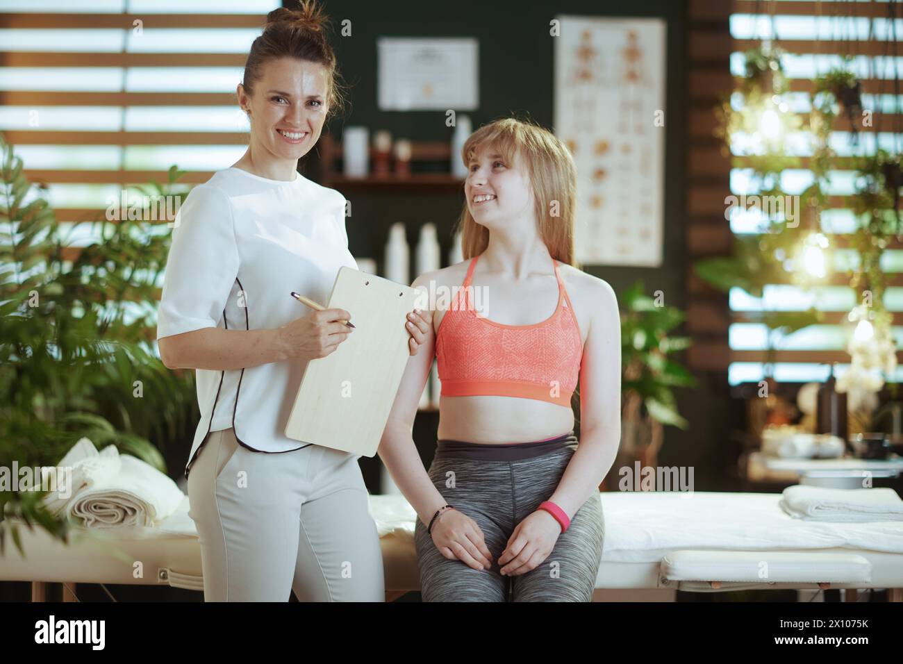 Healthcare time. happy massage therapist woman in massage cabinet with clipboard and teenage ...