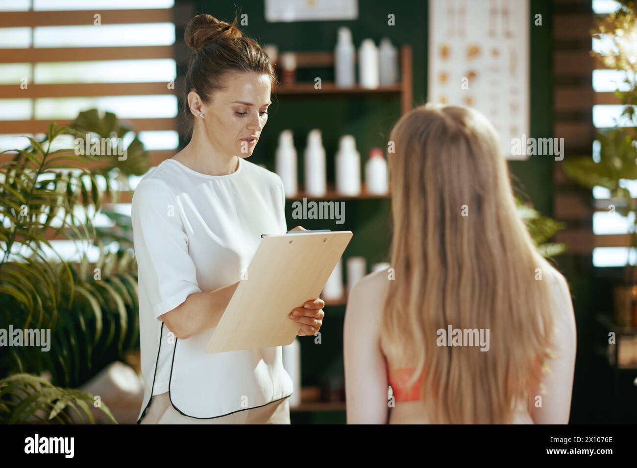 Healthcare time. concerned massage therapist woman in massage cabinet with clipboard and teenage ...