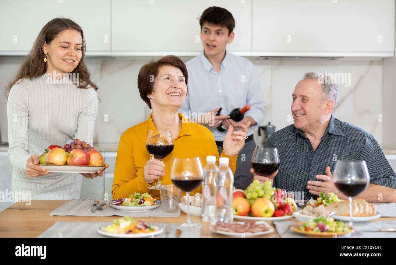 Father and mother together with adult children talking at dinner table ...