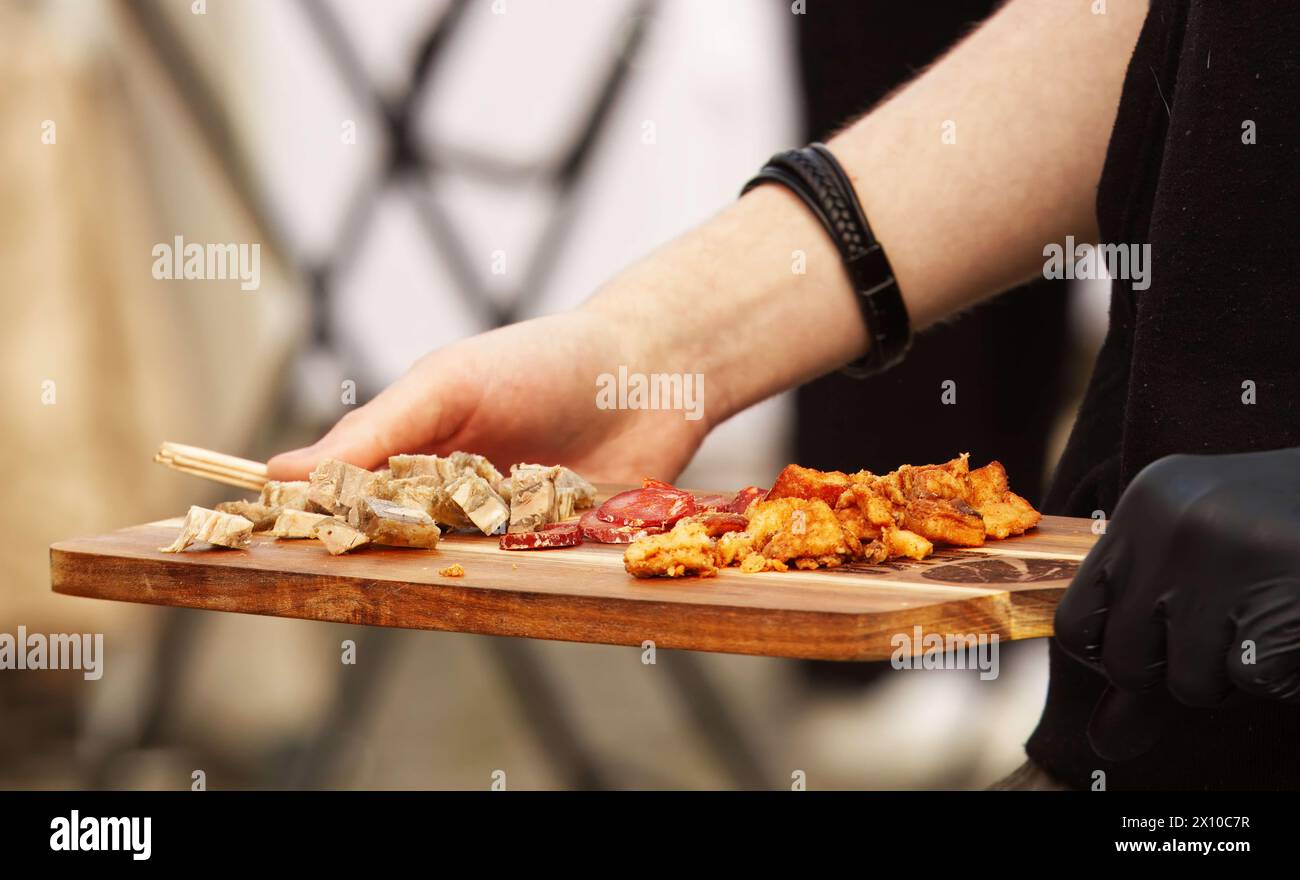Midsection body of a man offering a samples of meat dishes on a wooden ...