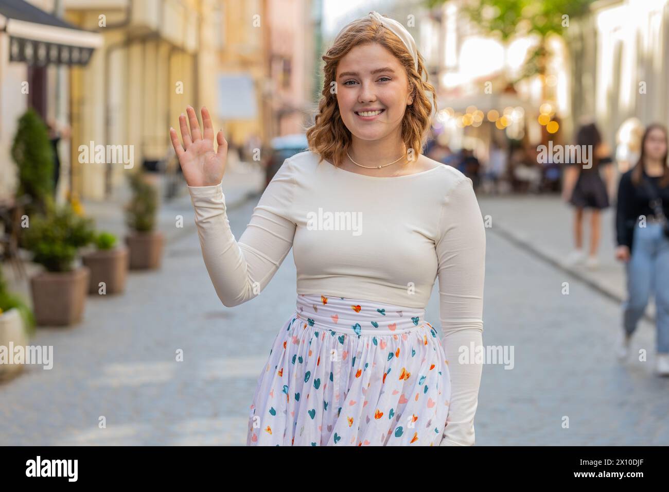 Hello. Redhead young woman in long dress smiling friendly at camera ...