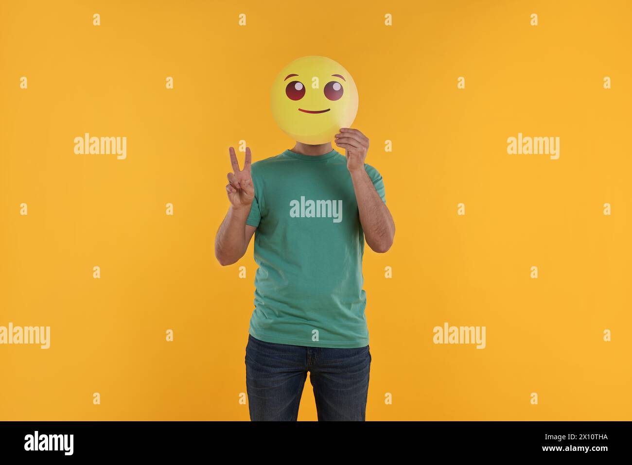 Man covering face with smiling emoticon and showing peace sign on ...