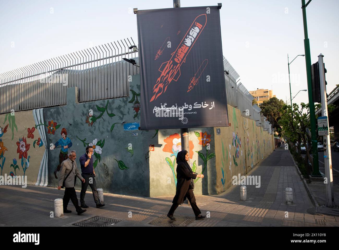 Tehran, Iran. 14th Apr, 2024. People walk past a poster depicting ...