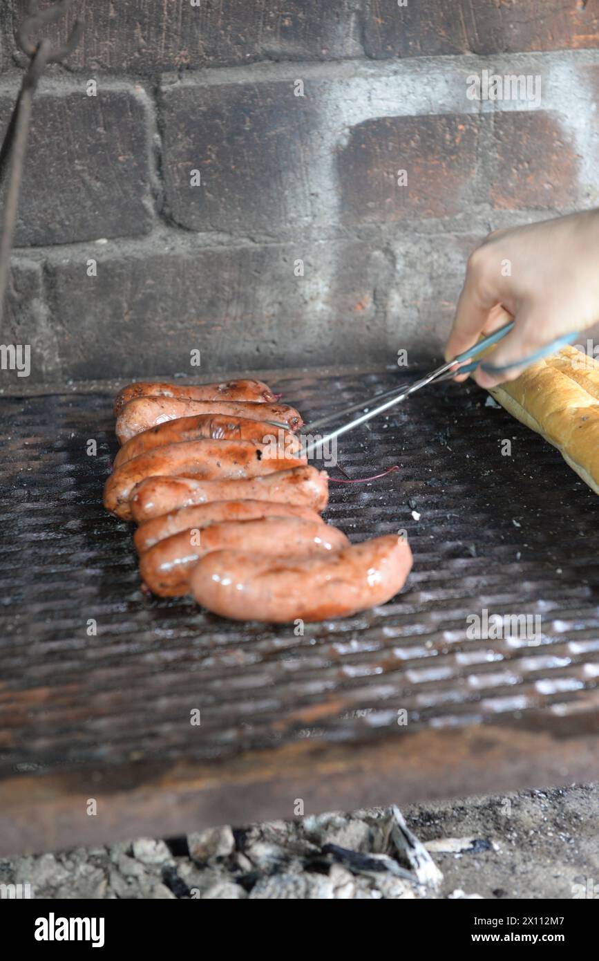 A person is cooking hot dogs on a grill. The hot dogs are on a metal ...