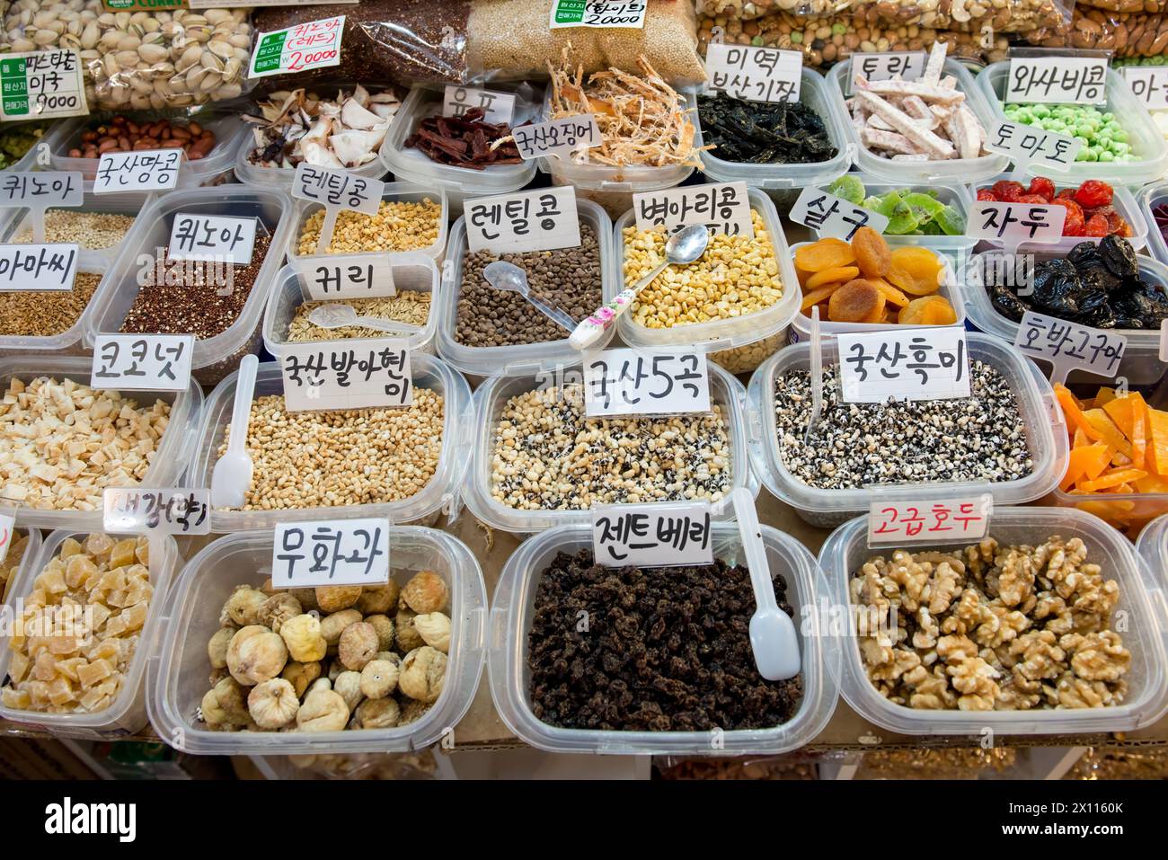 A variety of nuts and seeds are displayed in plastic containers. The ...