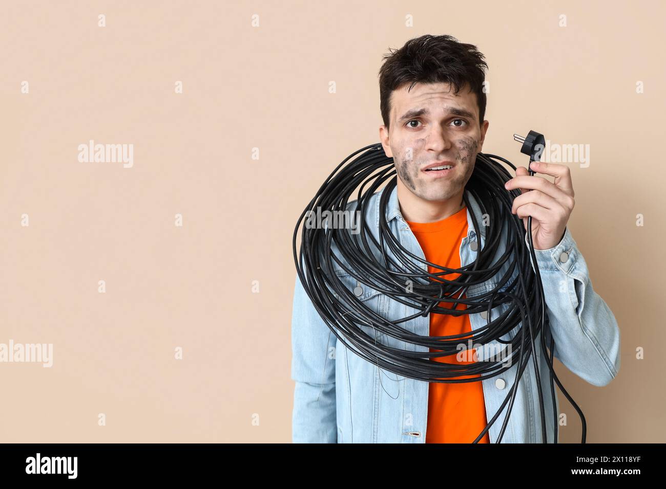 Electrocuted young man with burnt face and cable on beige background ...