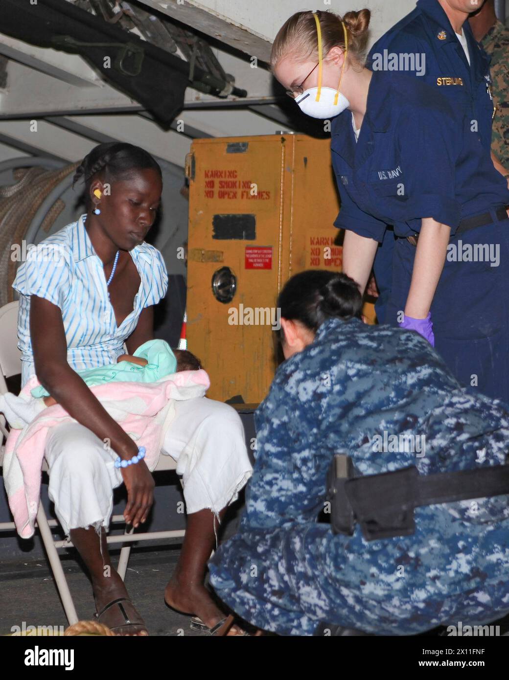 Sailors examine an injured Haitian woman with her child aboard ...