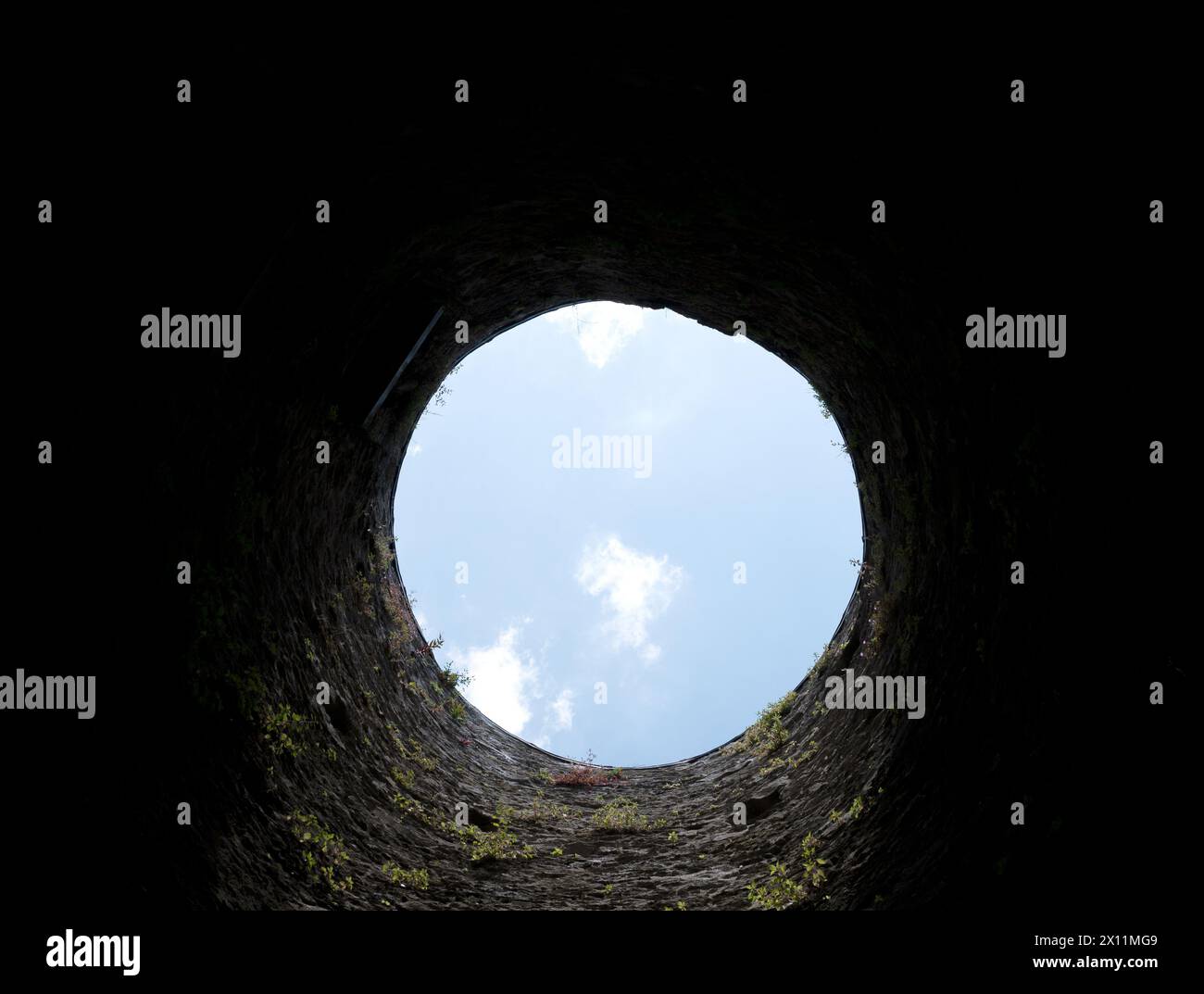 Stone well hole, old construction from inside, brick walls and blue sky ...