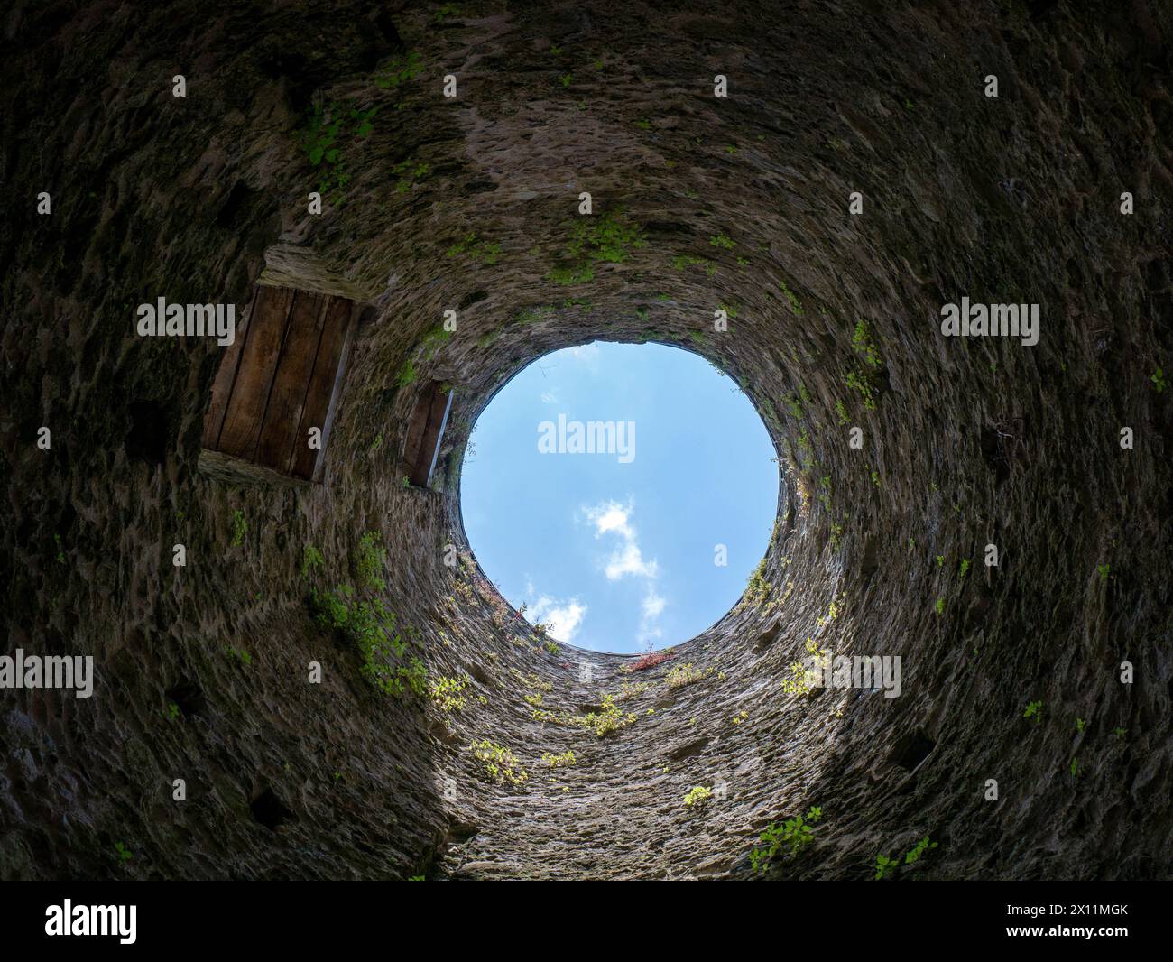 Stone well hole, old construction from inside, brick walls and blue sky ...