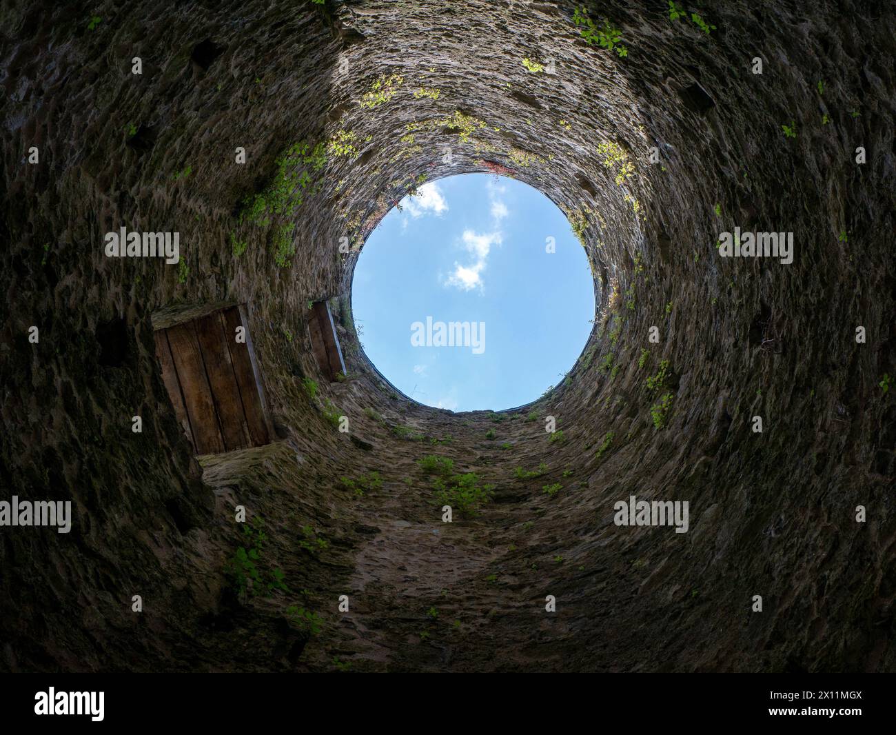 Stone well hole, old construction from inside, brick walls and blue sky ...