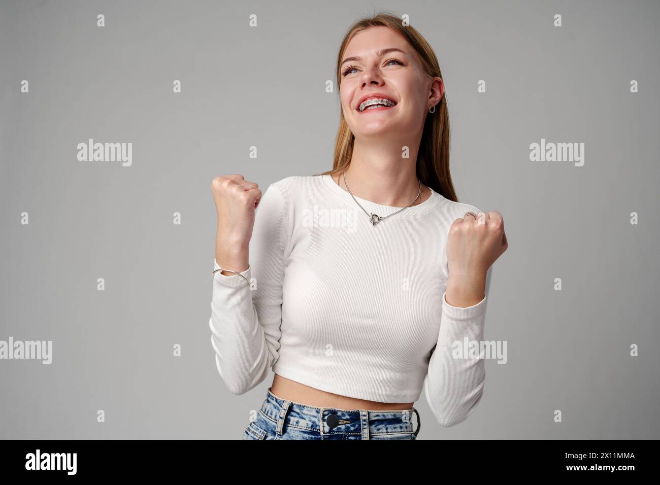 Smiling Young Woman in White Top Celebrating Success With Raised Fist ...