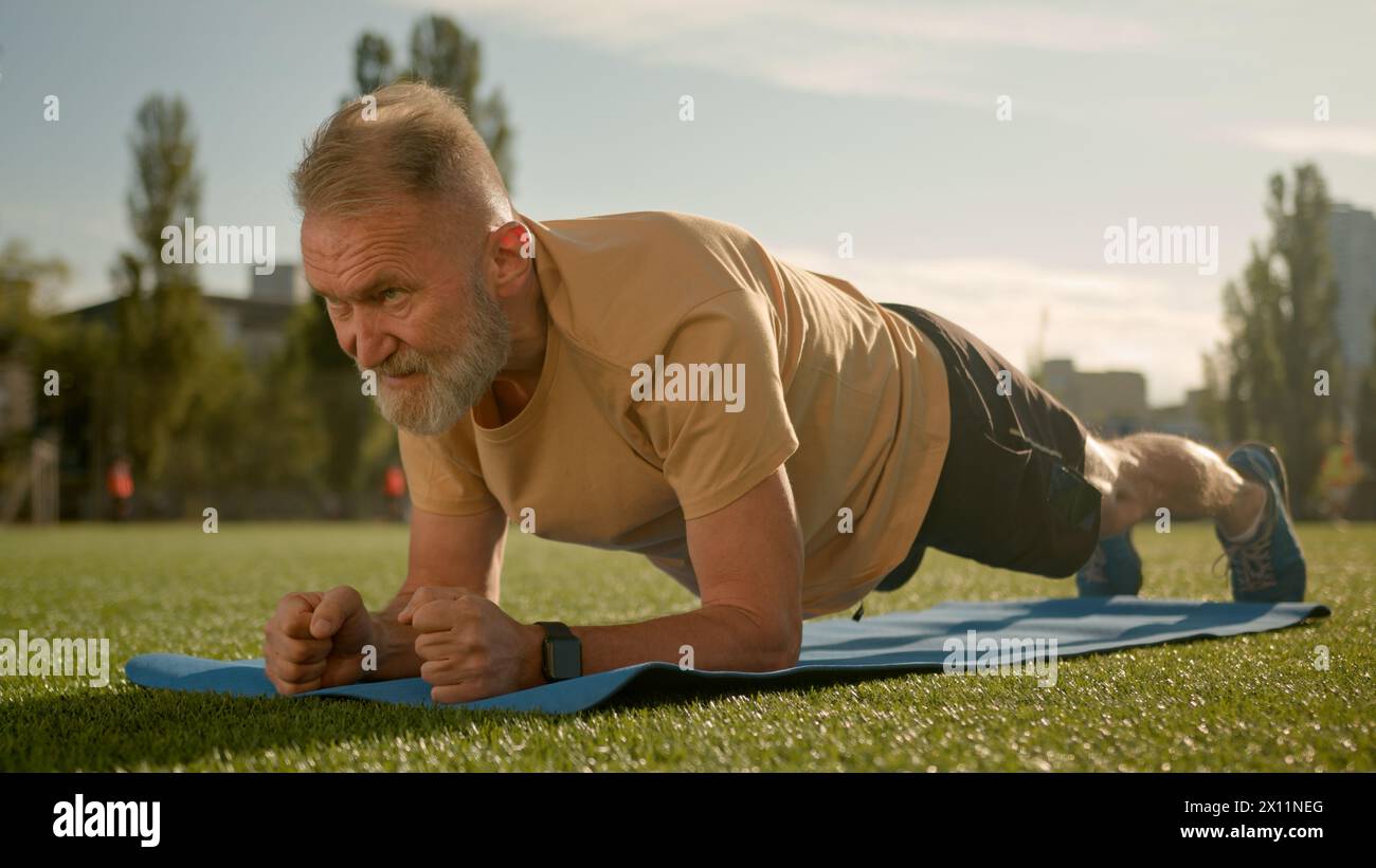 Caucasian old man in plank exercise workout training stadium city ...