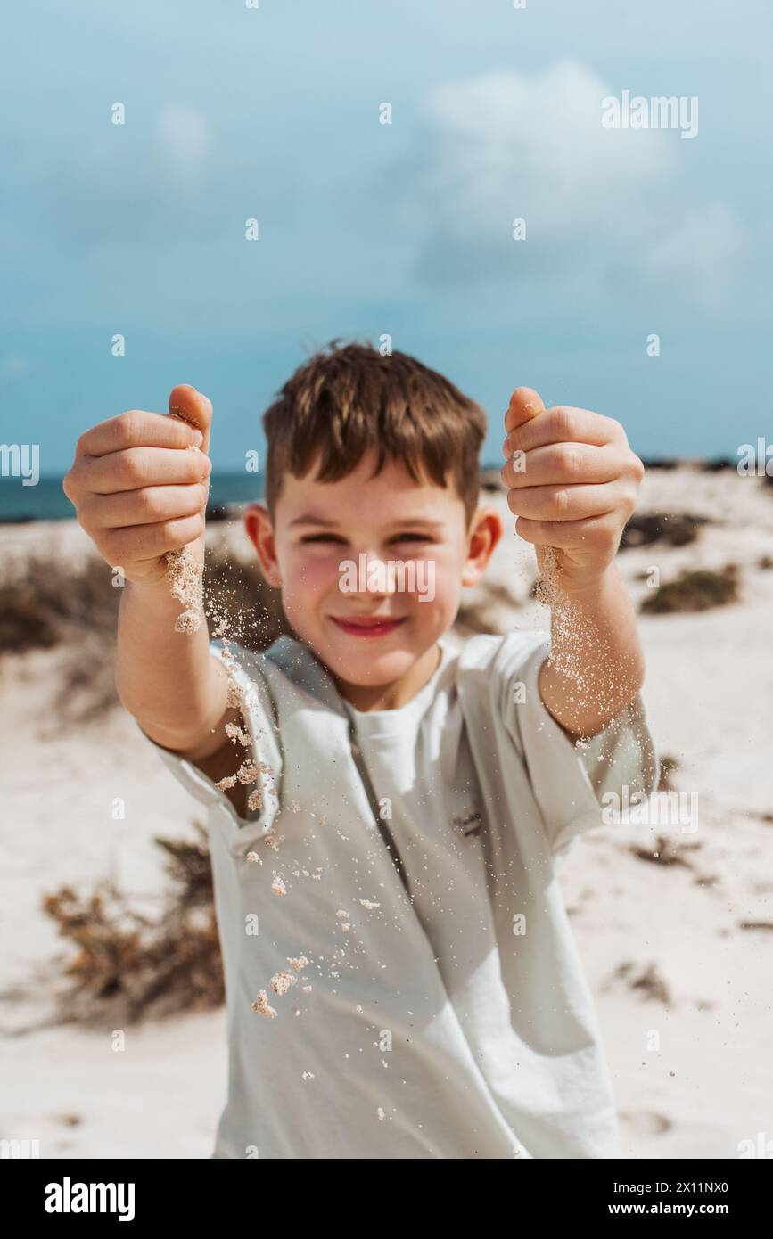 Boy with sand falling from his clnched fist, standing on beach. Family ...