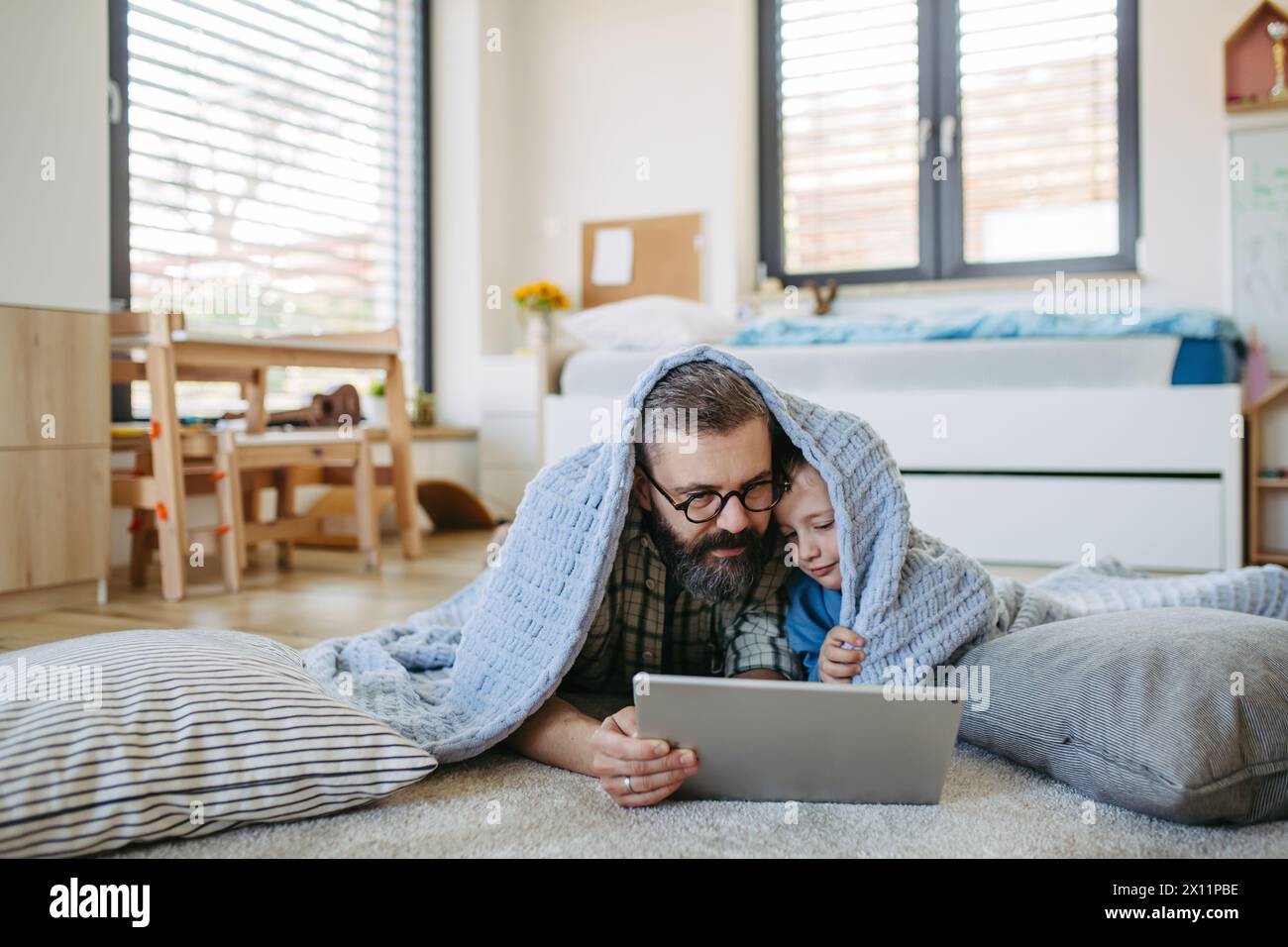 Little boy watching cartoon movie on tablet with father, lying under ...